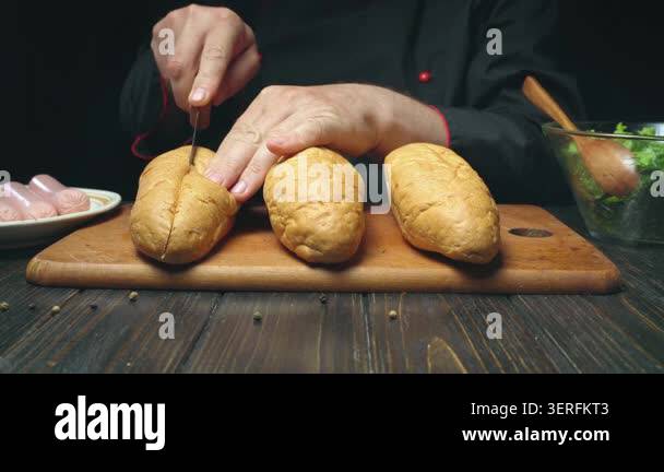 Chef in black attire skillfully slices open bread rolls for hot dogs on ...