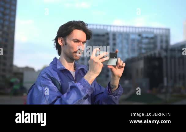 Young man in a blue jacket stands in the foreground using a smartphone ...