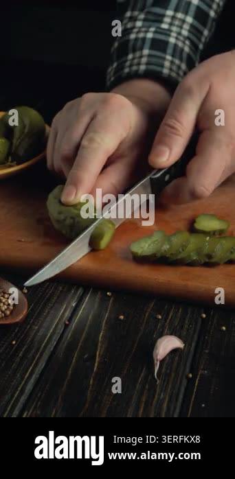 Hands skillfully slice pickles on a wooden cutting board, with garlic ...