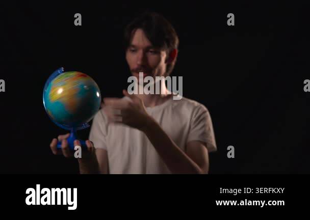 A young man stands against a black background, gently holding and ...
