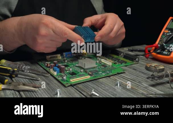 Hands of a technician carefully placing a heatsink onto a circuit board ...
