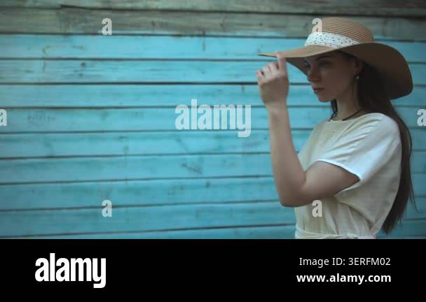 A woman stands in soft natural daylight, touching the brim of a wide ...