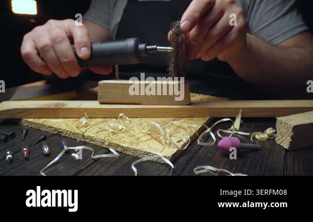 Hands of a male craftsman in an apron operate a rotary tool on a piece ...