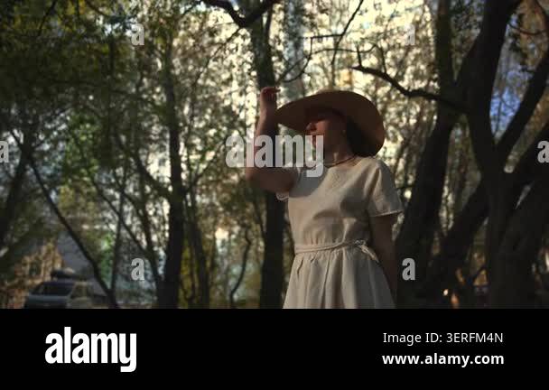 Woman in a light dress and wide brim hat poses gracefully among tall ...