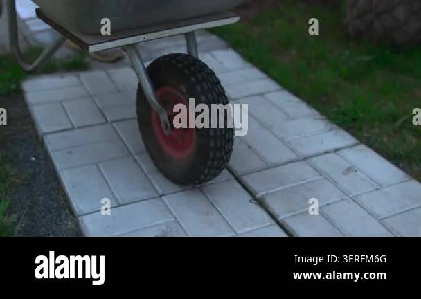 Close-up of a single wheelbarrow wheel resting near a light stone path ...