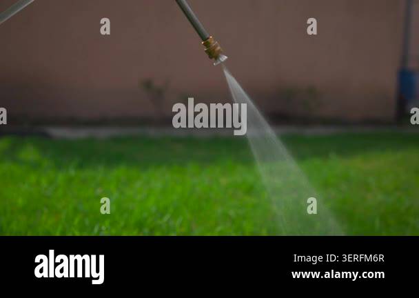 Close-up of a sprinkler nozzle spraying water across bright green grass ...