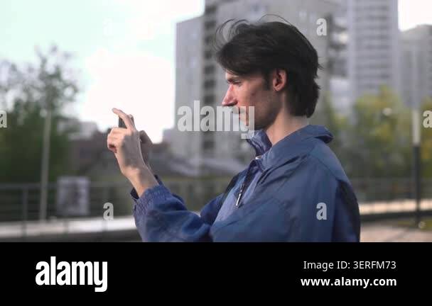 A young man in a blue jacket stands in side profile while using a ...