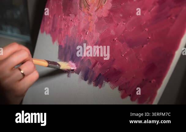 Close-up of a hand applying thick magenta and purple paint with a brush ...