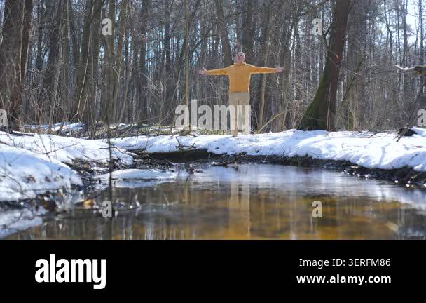 Man practicing breathing exercises by forest stream in early spring ...