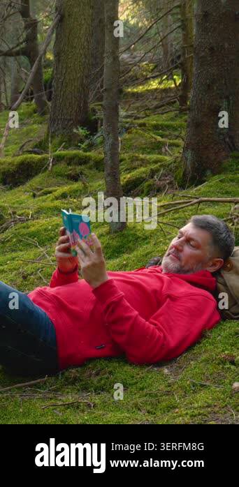Man reading book while relaxing on moss in peaceful forest wilderness ...