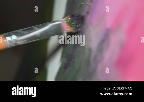 Close-up of a paintbrush spreading bright pink paint across a textured ...