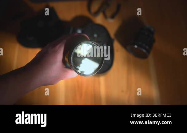 A hand holds a bright flashlight aimed toward the viewer above a wooden ...
