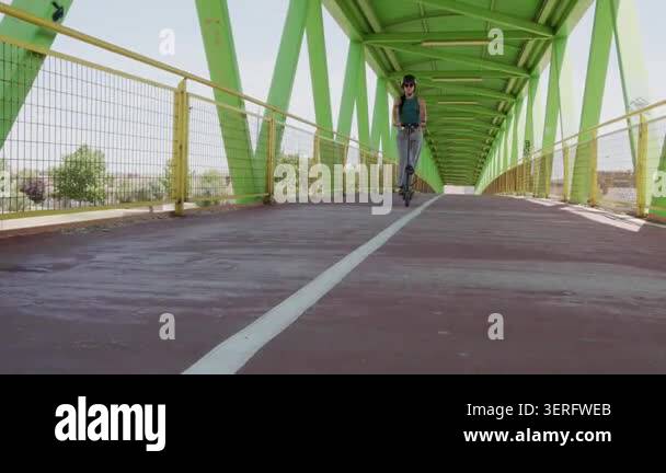 Young woman commuting on an e-scooter on a bike lane crossing a bright ...