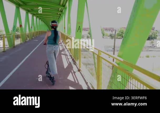 Rear view of a woman on an electric scooter crossing a modern green ...