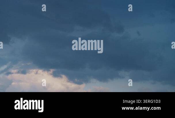 Dark storm clouds spread across a blue sky above a lighter cloud bank ...
