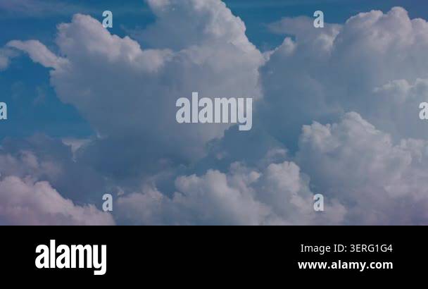 Large white cumulus clouds move across a clear blue sky creating a ...