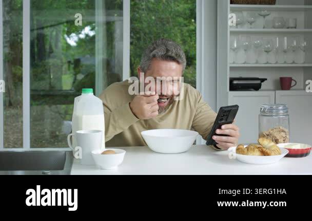 Man enjoying cereal breakfast and smartphone call. Man having breakfast ...
