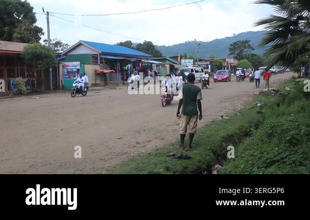 Busy street scene with people riding motorcycles and cars on a dirt ...