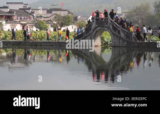 People walking across stone bridge over water with reflections of ...