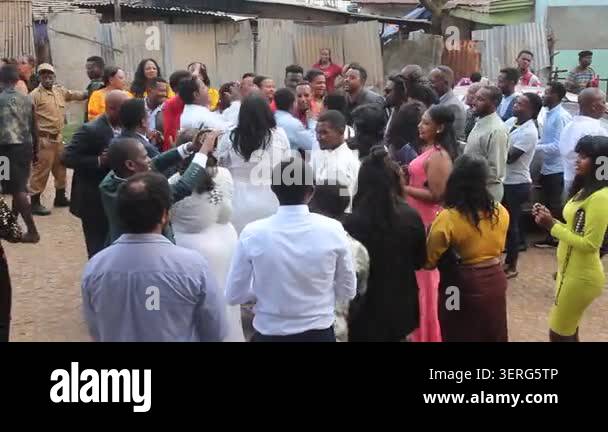 A large group of people are gathered outdoors, some dancing and ...