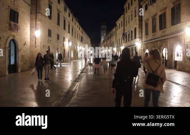People walking on a wet cobblestone street at night, illuminated by ...