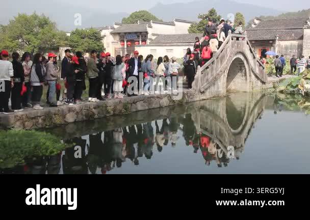 Group of people walking across stone bridge over calm water reflecting ...