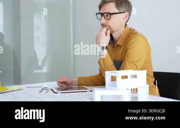Professional man in glasses and a mustard shirt sitting at a desk ...