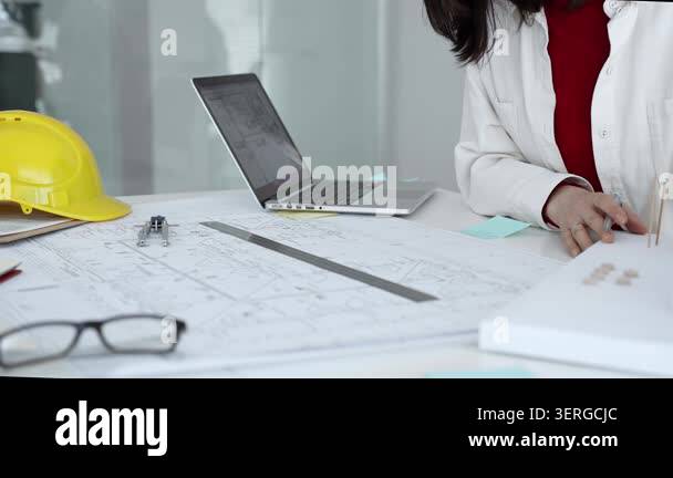 Woman working on blueprints, drawing with a pen, surrounded by design ...
