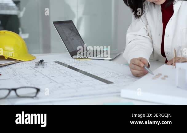 Woman working on blueprints, drawing with a pen, surrounded by design ...