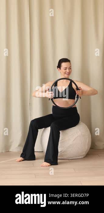 Pregnant woman holding pilates ring sitting on fitness ball during ...