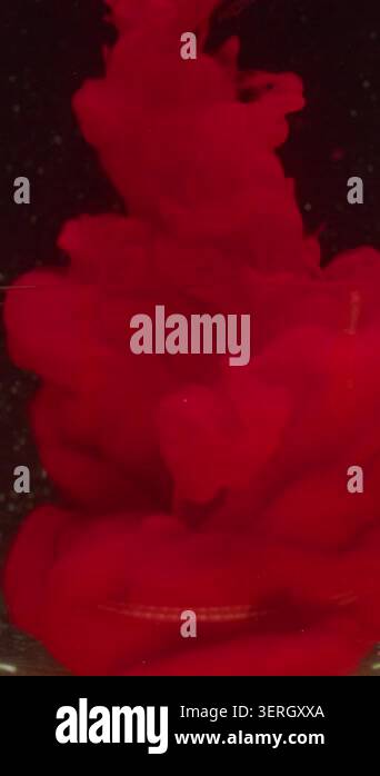 Vertical video. Red splash. Filling glass. Defocused vibrant color ink ...