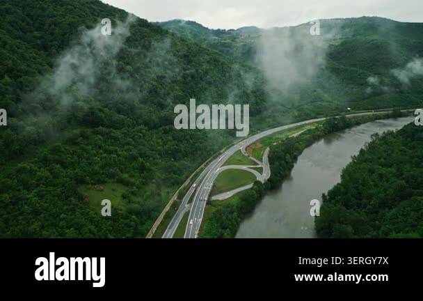 Drone shot of a winding river and empty highway running through a green ...