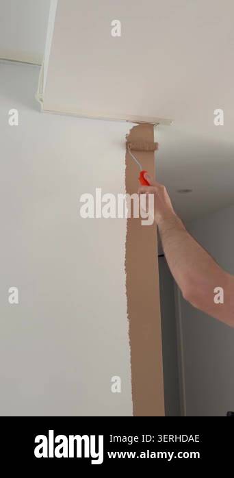 Painter applying warm beige paint with small foam roller to white wall ...