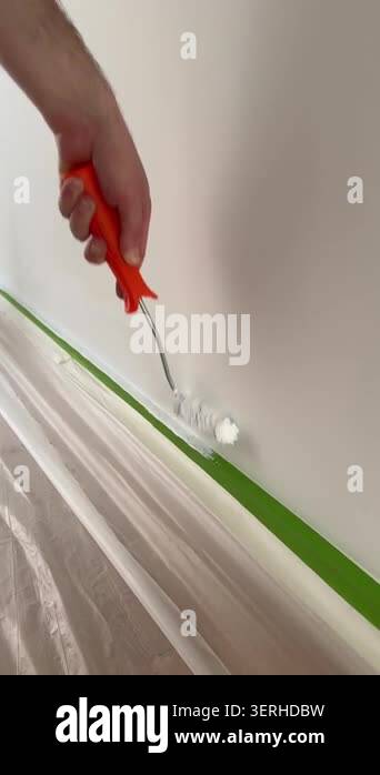 Hand using long handled mini foam roller to apply white paint along ...