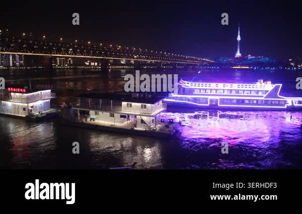 Night view of illuminated boats on a river with a bridge and tower in ...