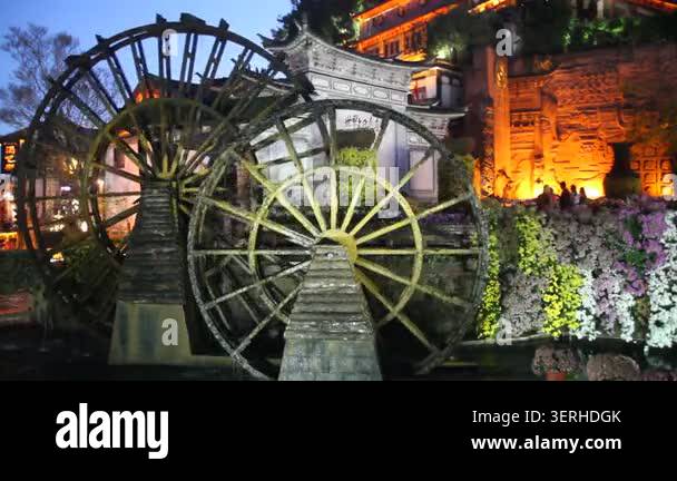 Two large wooden water wheels turn slowly beside a building with ...