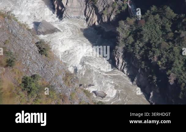 Aerial view of turbulent river flowing through rocky gorge with dense ...