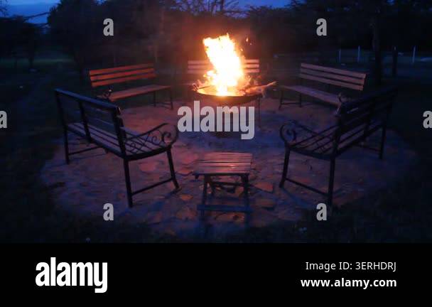 Campfire burning brightly at night surrounded by empty benches and a ...