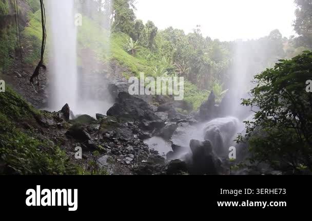 Wide shot of a lush jungle waterfall cascading down rocky cliffs into a ...
