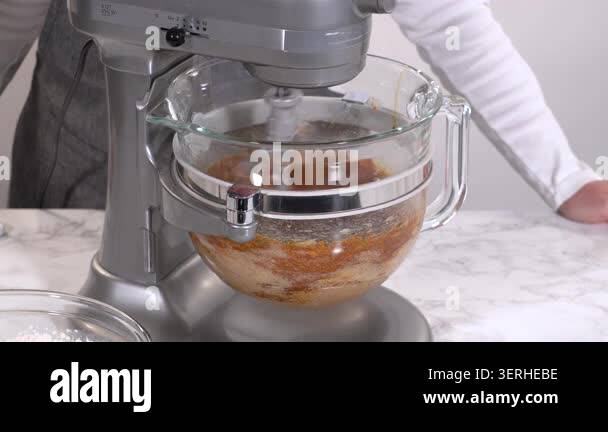 Hands pour dark liquid mixture into a stand mixer bowl already ...