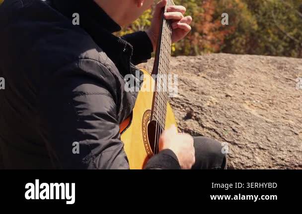 Close up hands of artist plays wooden acoustic guitar in autumnal park ...