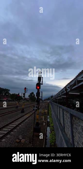 Vertical video of Train station platform under a metal roof. Red signal ...