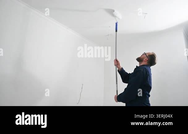 Technician applies white coating to ceiling in residential room ...