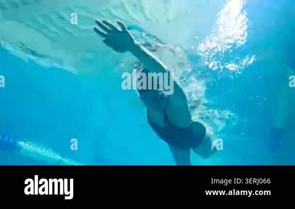 Female swimmer glides beneath surface during freestyle crawl in indoor ...