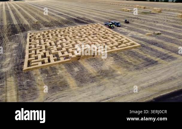 Intricate maze from hay bales stretches on agricultural field. Tractors ...