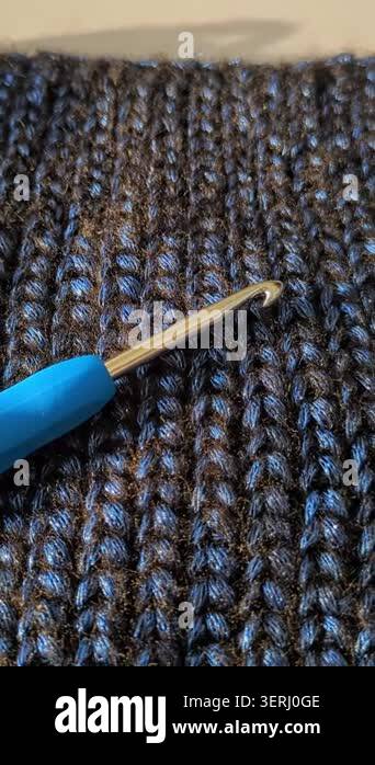 Crochet hook on dark blue textured, crochet warm chunky fabric. Close ...
