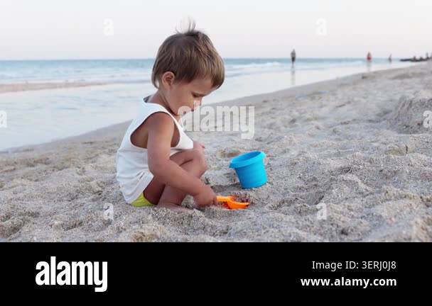 A little cheerful, enthusiastic boy plays with his toys on a sea sandy ...
