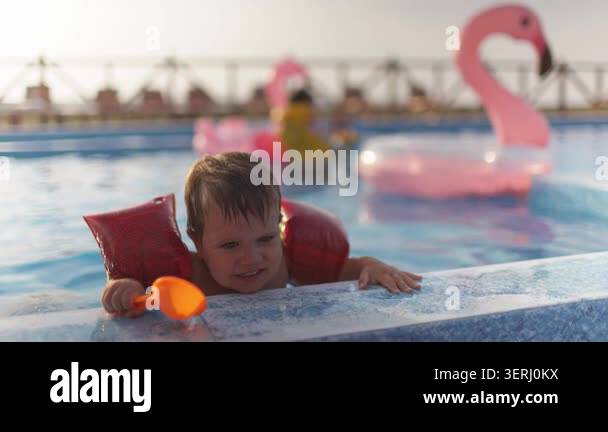 A little boy with colored armbands and disgruntled face, tries to get ...