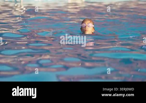 A little girl in a bright pink swimsuit with transparent black goggles ...