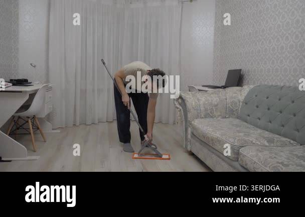 Cleaning living room. Homeowner tidying up with mop. Casual homeowner ...